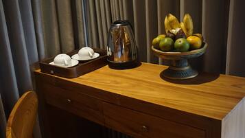 Uma mesa de madeira com uma cafeteira, um tabuleiro com duas chávenas brancas e uma fruteira com bananas, limões e limas.