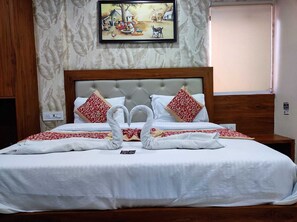 Cama bem arrumada com colcha branca, duas almofadas estampadas em vermelho e dois cisnes feitos de toalhas.