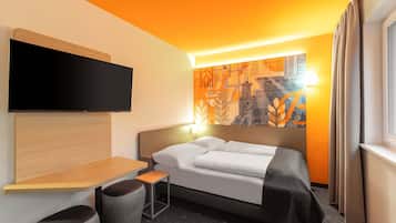 Quarto de hotel moderno com cama, televisão de tela plana, mesinha e uma cadeira.
