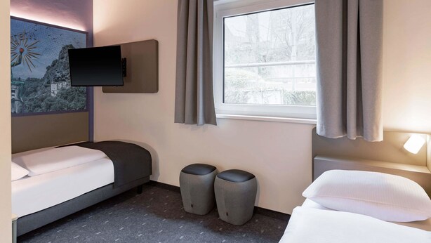 Quarto de hotel com duas camas, televisão na parede, janela com cortinas e um pequeno alto-falante.