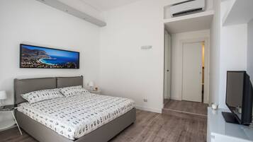 Quarto moderno com cama, televisão e pintura de uma paisagem costeira.