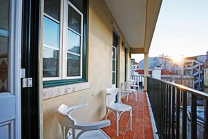 Varanda com cadeiras brancas e chão de azulejos, com vista para a cidade.