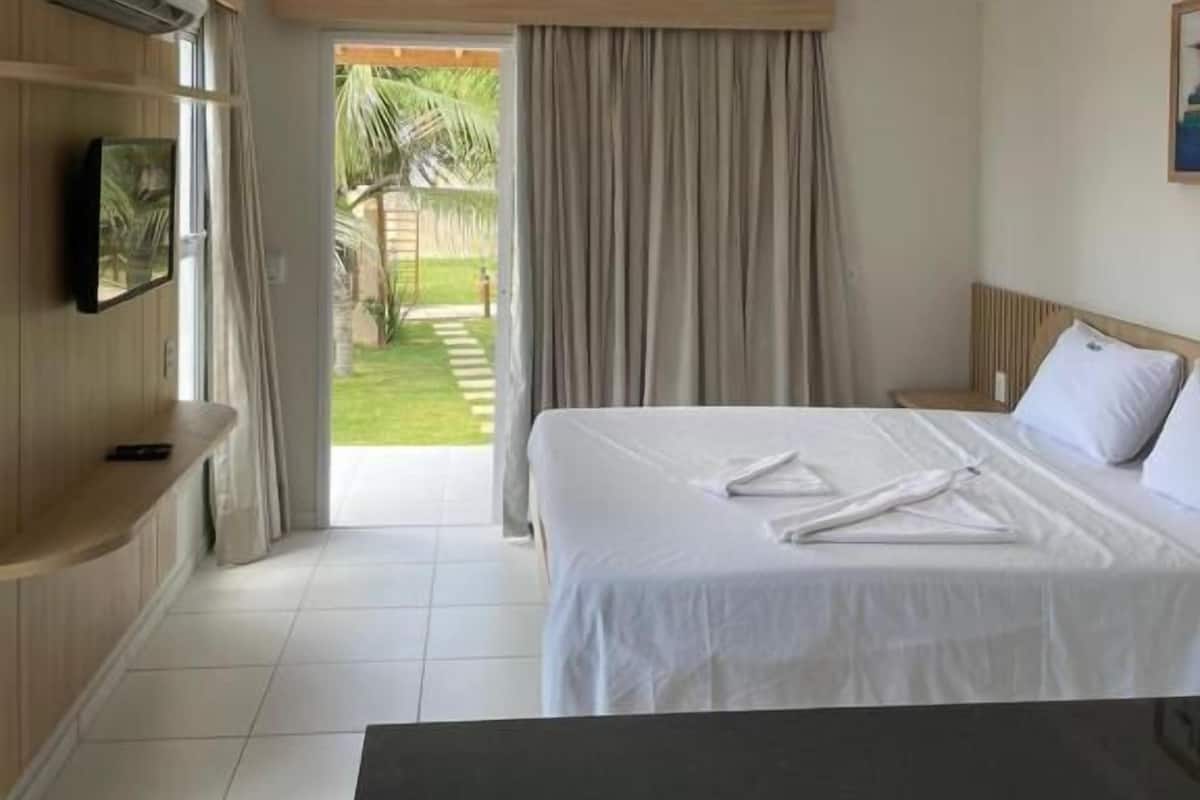 Quarto de hotel com uma cama, uma televisão na parede e vista para um jardim.
