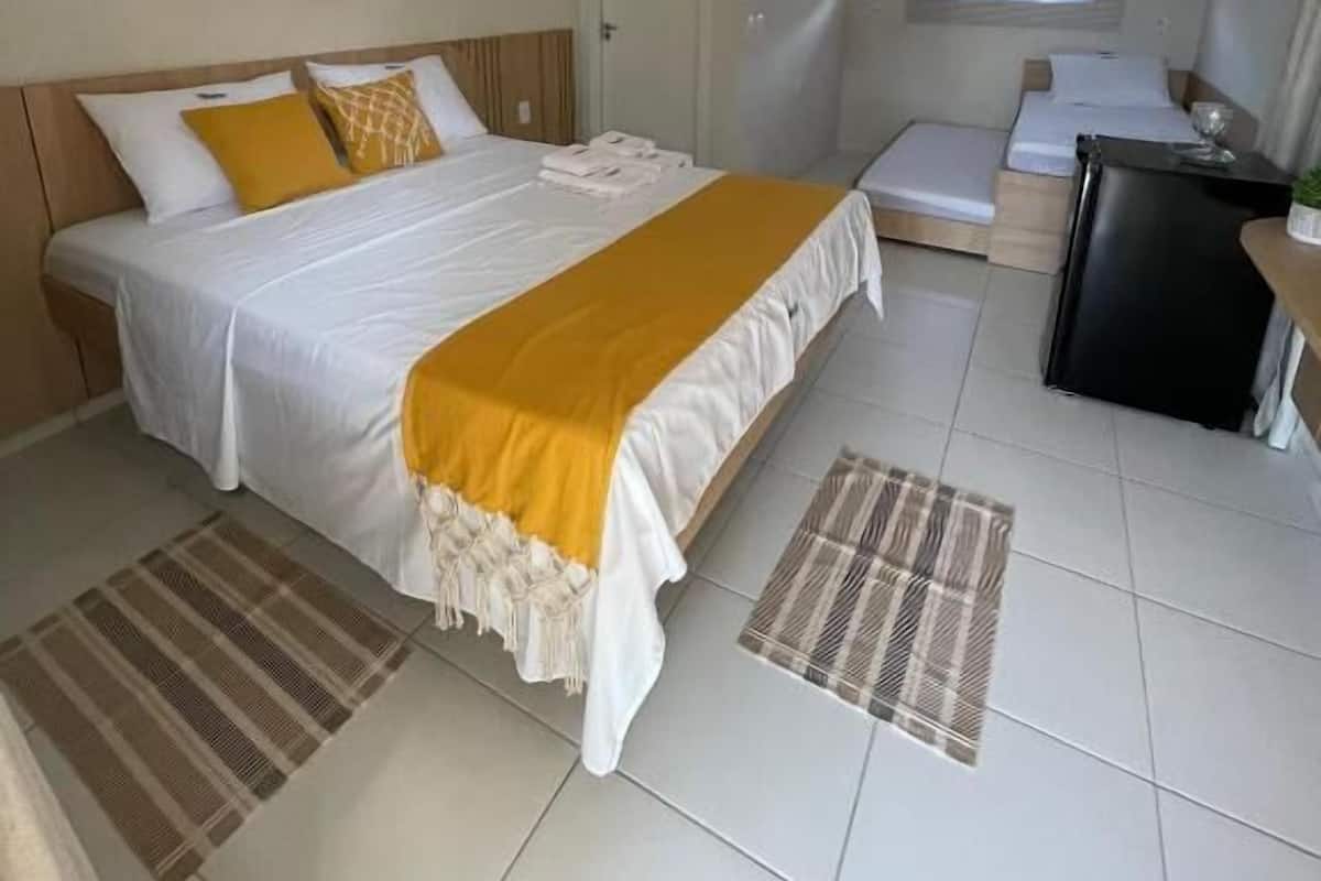 Quarto de hotel com cama, escrivaninha, cadeira, janela e porta.