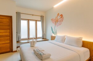 Quarto de hotel com uma cama grande, janela com cortinas, cabeceira de madeira e pintura floral na parede.