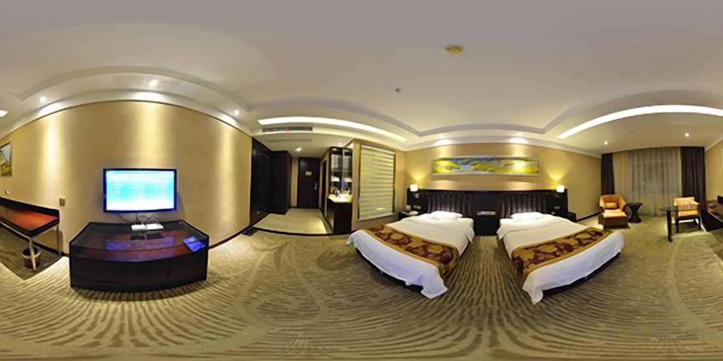 Quarto de hotel com duas camas, televisão, escrivaninha e área de estar.