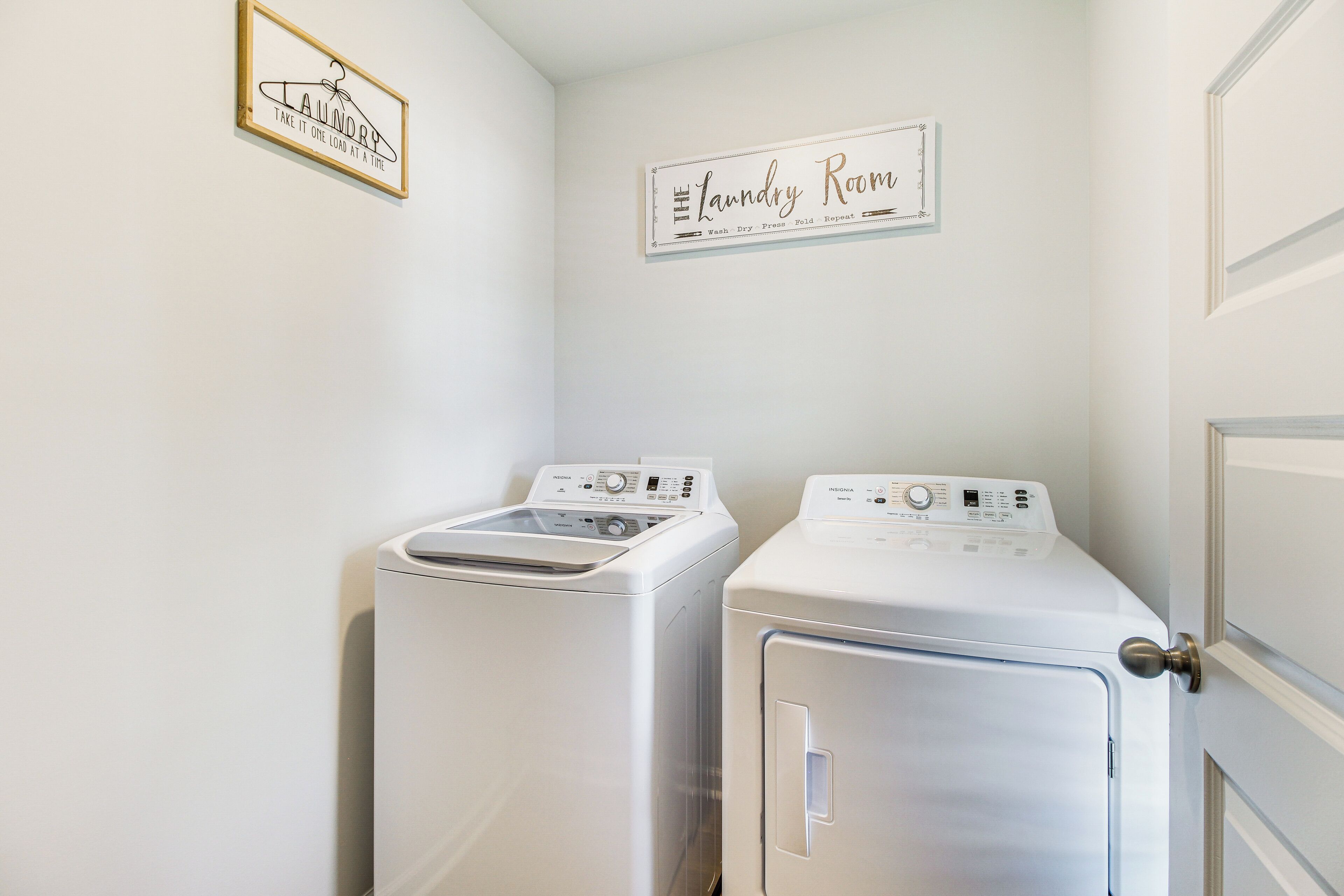 Uma lavanderia com duas máquinas de lavar brancas e uma placa acima delas com a inscrição THE Laundry Room.