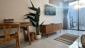 Uma sala de estar moderna com uma mesa de jantar de madeira, uma grande planta em vaso, um armário de madeira e uma porta de vidro que dá para o exterior.