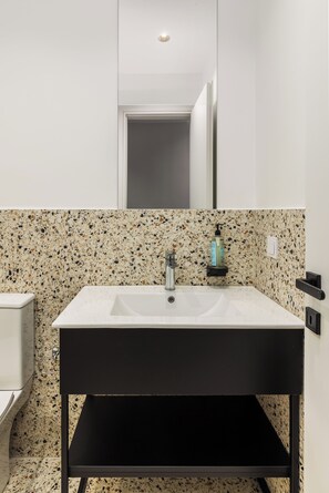 Casa de banho com lavatório branco, bancada preta e painel de azulejos com manchas.