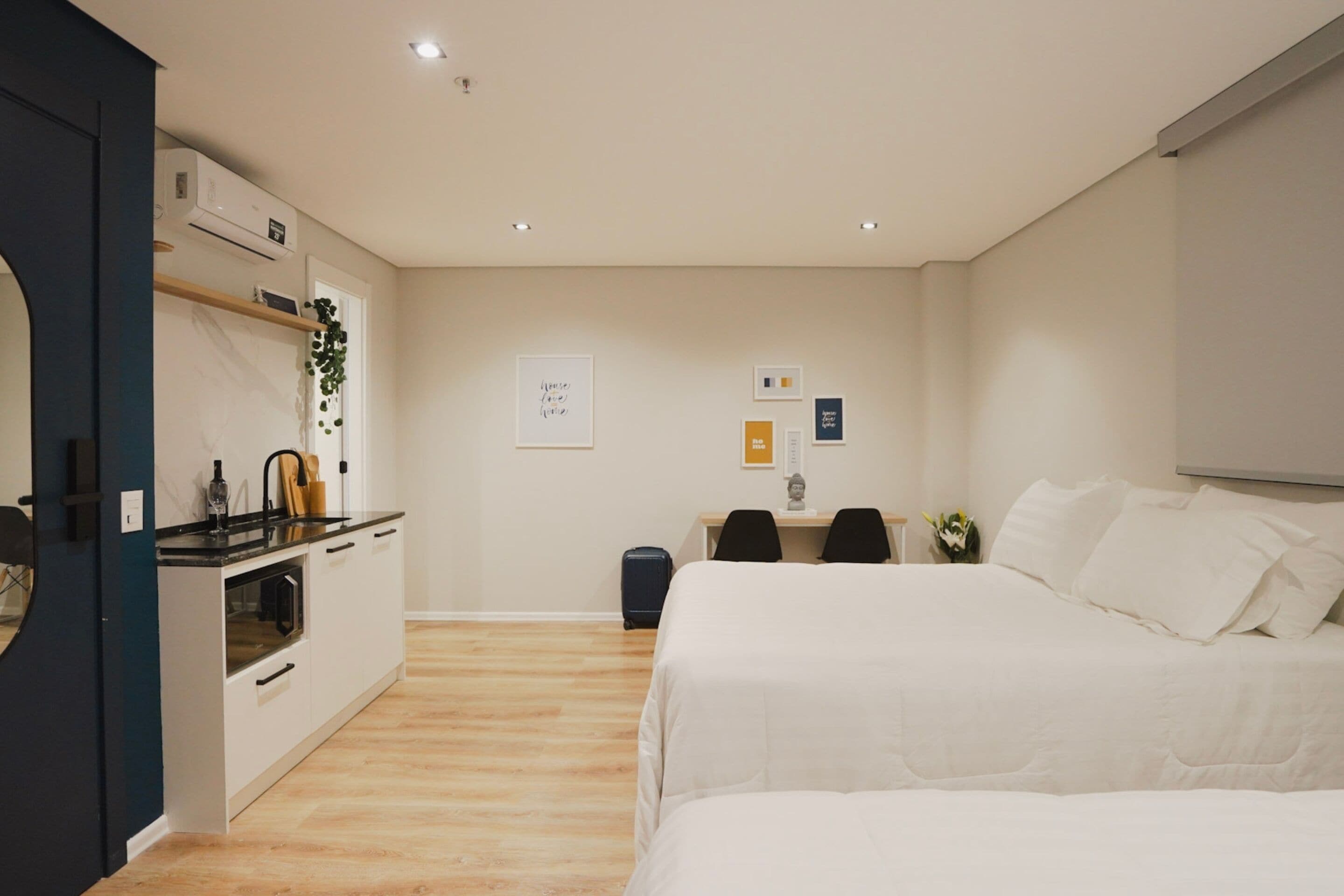 Quarto de hotel moderno com cozinha compacta, cama e escrivaninha.