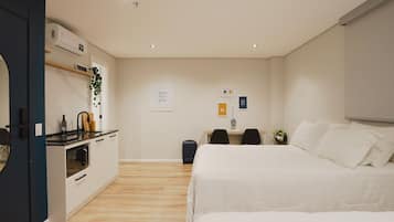 Quarto de hotel moderno com cozinha compacta, cama e escrivaninha.