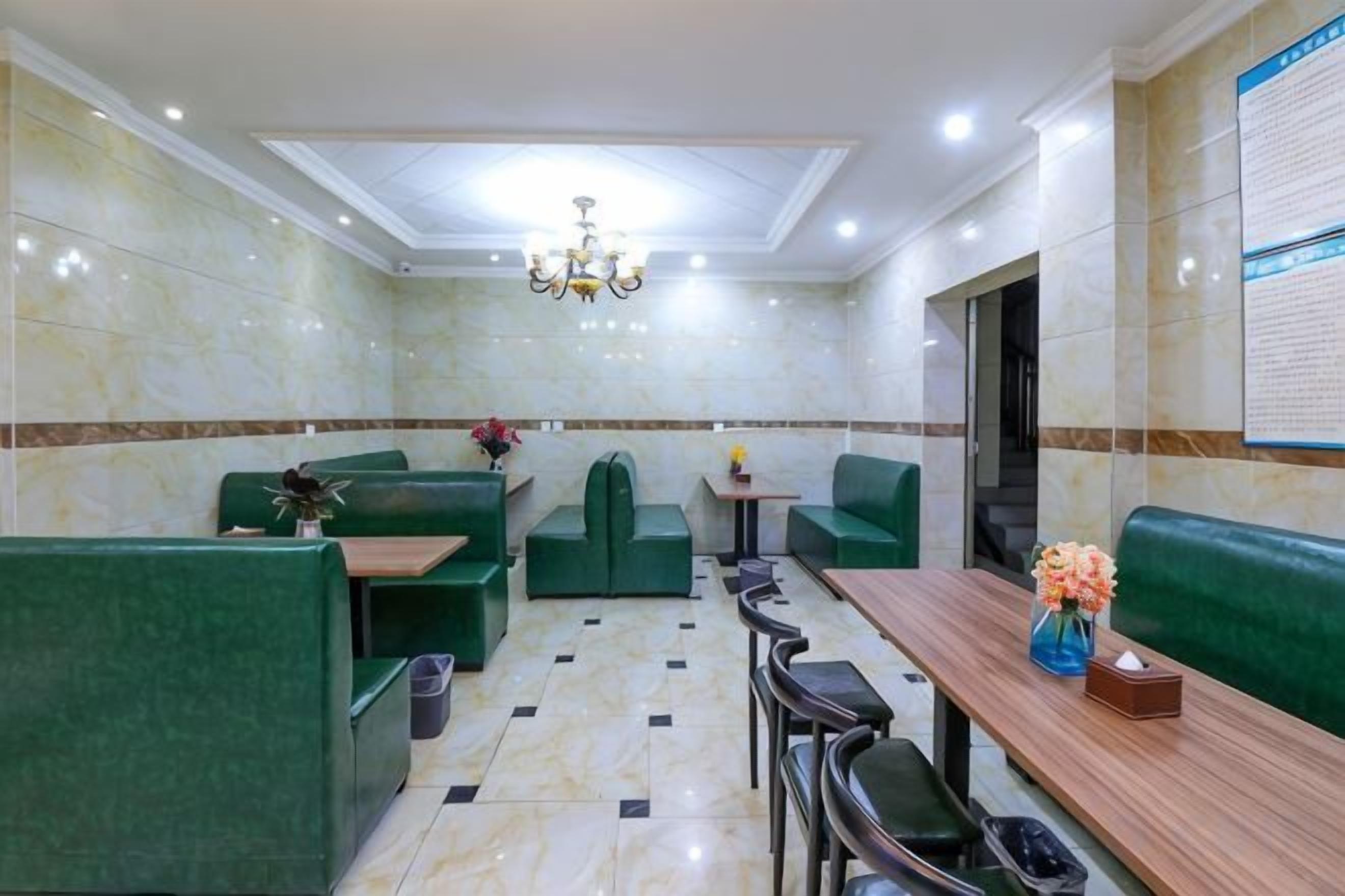 Um saguão de hotel com assentos verdes, um balcão de recepção de madeira e um candelabro.
