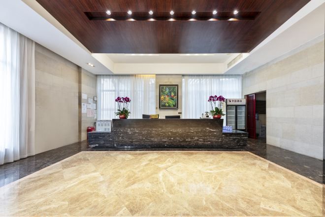 Um hall amplo com piso de mármore, balcão de recepção e plantas em vasos.
