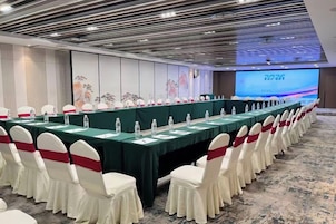 Uma sala de conferências com uma mesa comprida, cadeiras e uma tela grande.