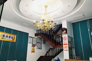 Um saguão de hotel com um lustre imponente, uma escadaria e um balcão de recepção.