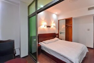 Quarto de hotel com cama, luminárias de cabeceira, guarda-roupa e escrivaninha.