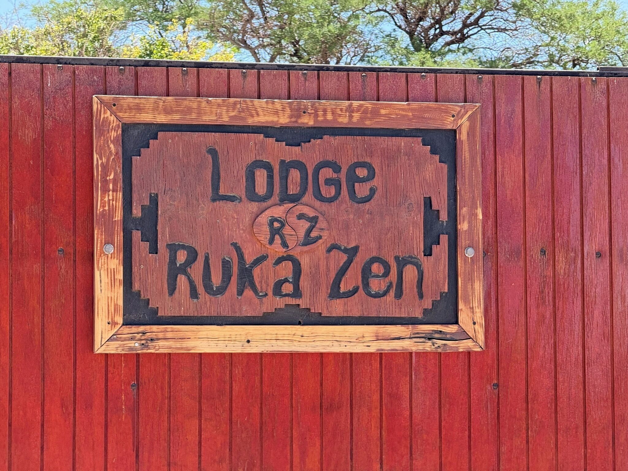Uma placa de madeira com o texto "Lodge RZ Ruka Zen" em uma parede de madeira vermelha.