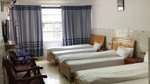 Quarto de hotel com três camas de solteiro, cabeceiras de madeira, uma mesa com cadeira e uma janela com cortinas.