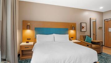 Quarto de hotel com uma cama grande, duas mesas de cabeceira, um criado-mudo, uma cadeira, um espelho e uma porta.