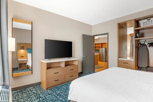 Quarto de hotel com cama, televisão, guarda-roupa e banheiro visível por uma porta aberta.