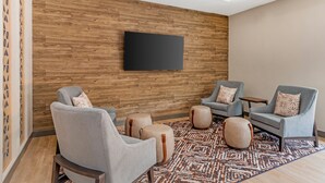 Uma sala de estar moderna com parede de madeira, TV de tela plana, poltronas cinzas, pufes e um tapete estampado.