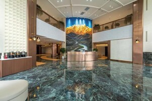 Um saguão de hotel com balcão de recepção, piso de mármore e um mural de montanhas.