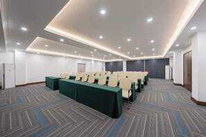 Sala de conferências com fileiras de cadeiras, piso coberto por carpete e iluminação embutida no teto.