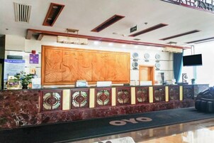 Bancada de recepção com painel de madeira, balcão de mármore e tela de televisão.