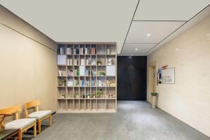 Uma área de recepção com estante, assentos e uma porta escura.