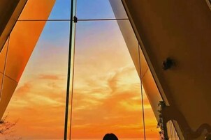 Quarto com uma janela grande, uma cama e vista para o pôr do sol.