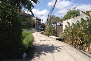 Estrada estreita ladeada por vegetação e um muro de concreto, que leva a um edifício com entrada visível.