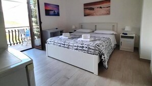 Quarto com cama, duas mesas de cabeceira, um criado-mudo, janela com vista e porta que dá para uma área externa.