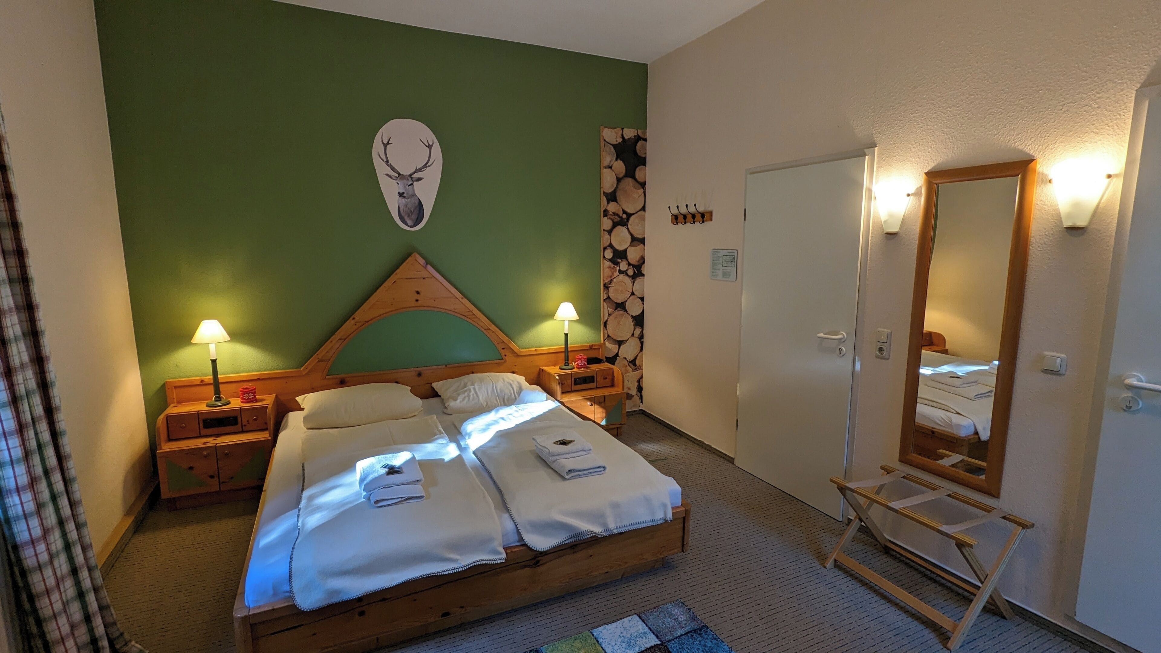 Quarto com cama, duas mesas de cabeceira, um espelho e um painel decorado com cabeça de veado.