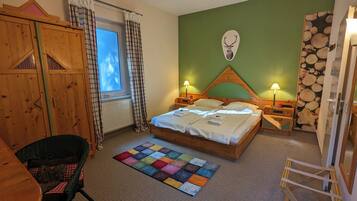 Um quarto com cama de madeira, um tapete colorido, guarda-roupa de madeira, uma janela com cortinas e um chifre de veado decorativo fixado na parede.