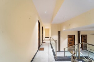 Corredor moderno de hotel com guarda-corpo de vidro, portas de madeira e piso ladrilhado.