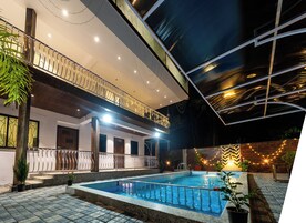 Uma área de piscina moderna ao ar livre, com um terraço de dois andares, plantas em vasos e luzes de Natal.