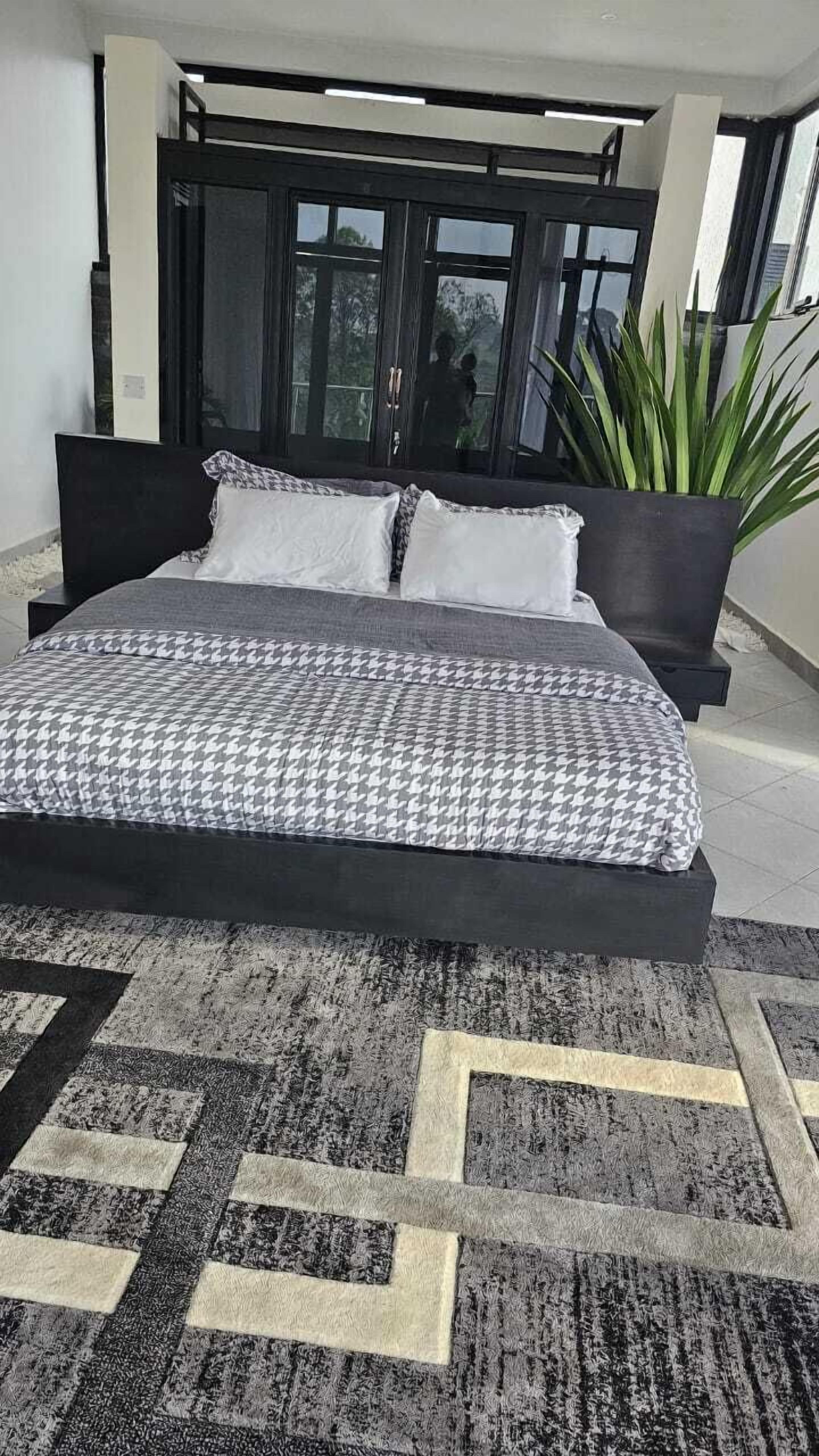 Quarto moderno com uma cama grande, cabeceira escura e vista para o exterior através de uma porta de vidro.