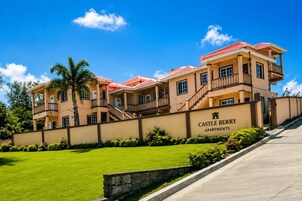 Um edifício de vários andares com varandas, identificado como 'Castle Berry Apartments', cercado por um gramado bem cuidado e um céu limpo.