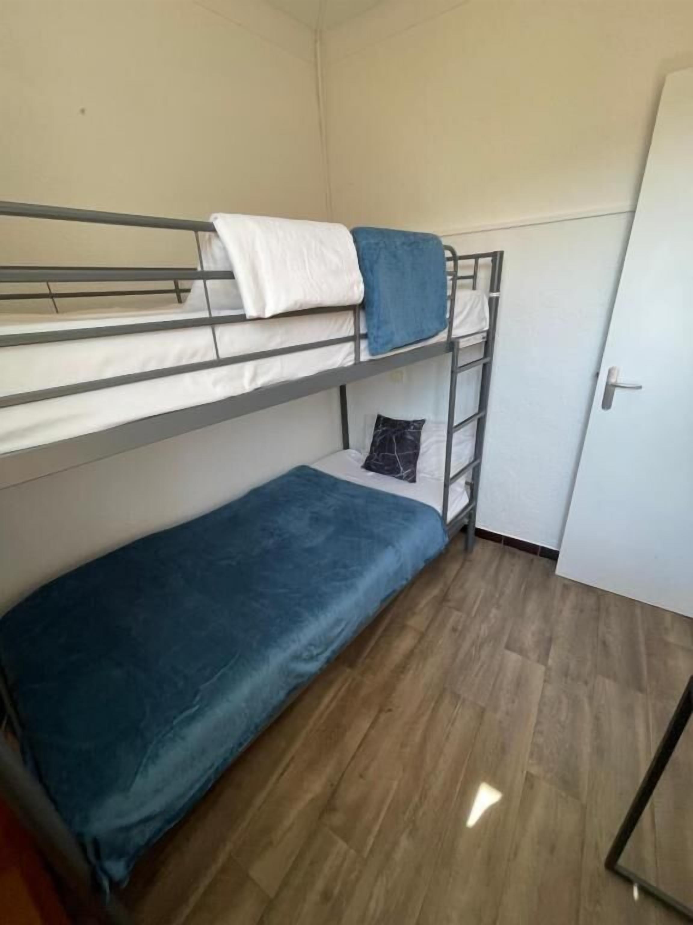 Quarto pequeno e compacto com uma cama beliche e uma cama individual. Há uma porta do lado direito e um pequeno armário na parede.