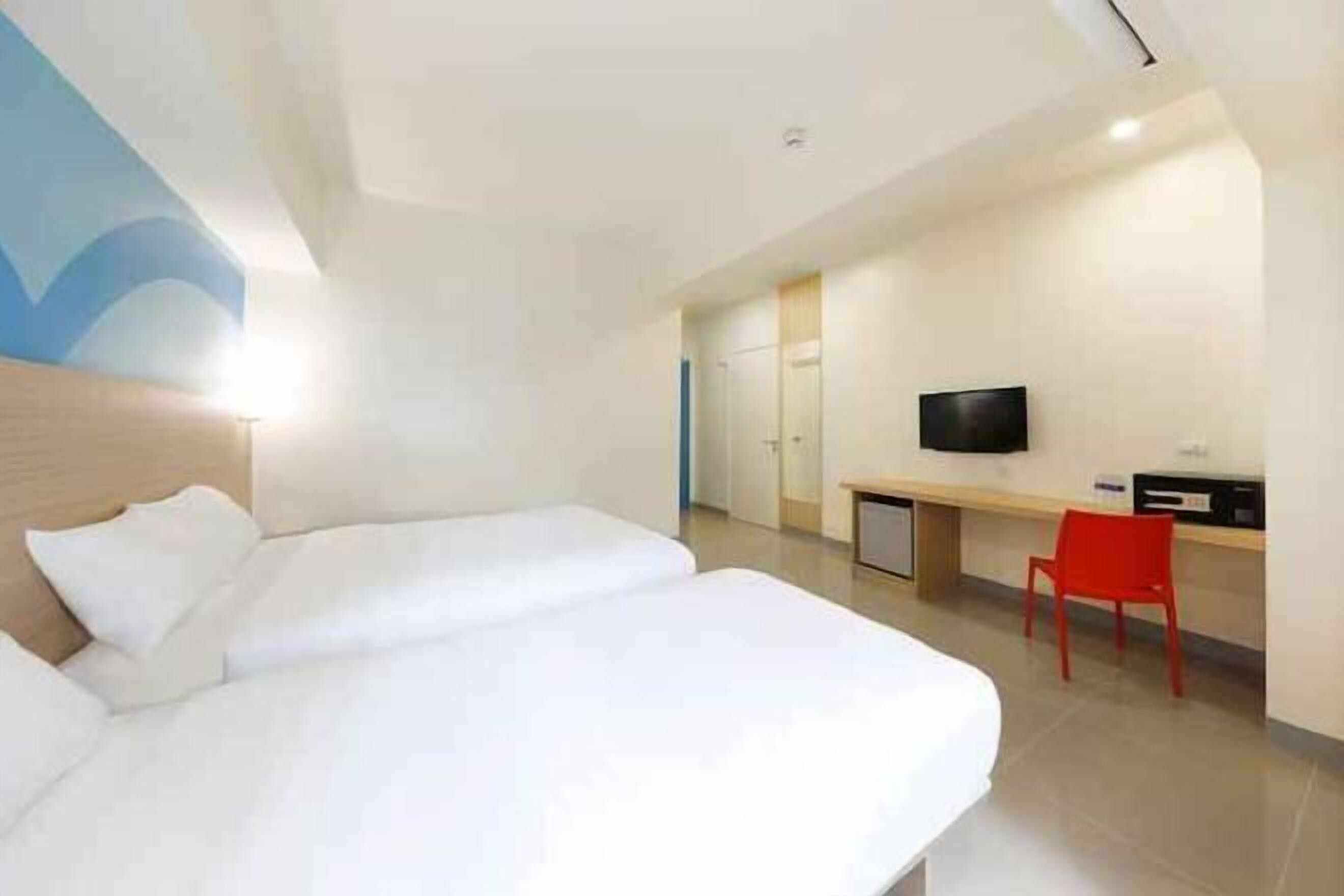 Quarto de hotel com duas camas, uma escrivaninha, uma televisão e uma cadeira vermelha.