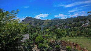 Paisagem montanhosa sob um céu claro, com vegetação exuberante e alguns edifícios ao longe.