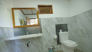 Casa de banho com parede revestida a mármore, lavatório branco, espelho, sanita e um lixo.