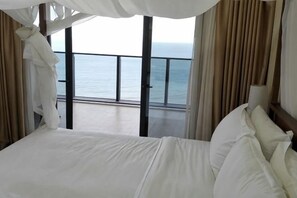 Uma cama grande com lençóis brancos, um dossel e vista para o mar através de uma varanda.