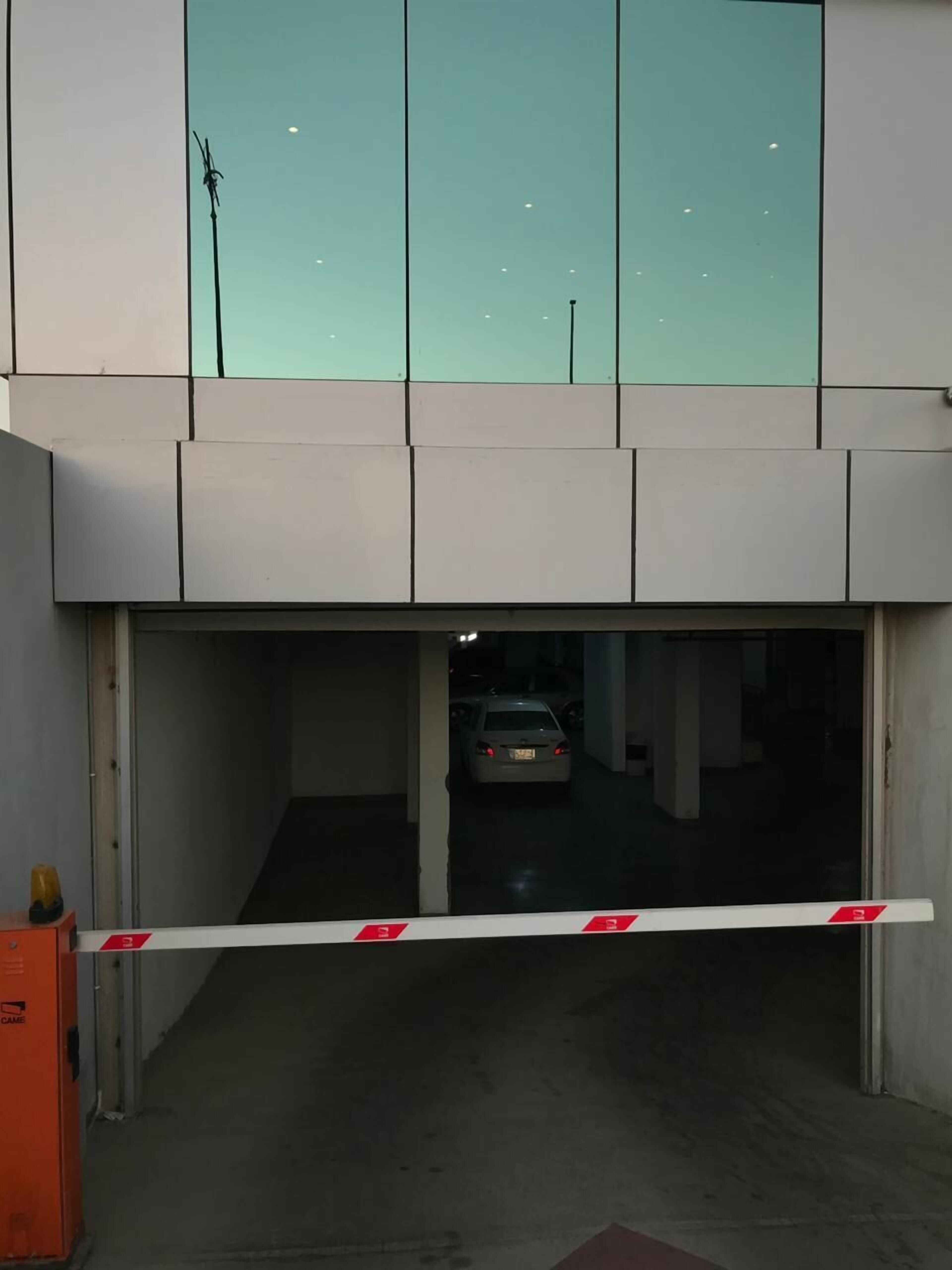 Entrada de um estacionamento com um carro no interior, um portão de segurança e vista do céu através do teto do edifício.