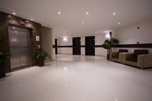 Um hall amplo com uma receção em mármore, área de receção, zona de estar com sofás e um elevador.