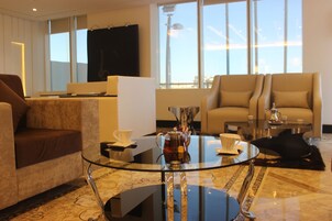 Uma sala de estar moderna com uma mesa de centro de vidro, sofás de couro e uma televisão de tela plana.