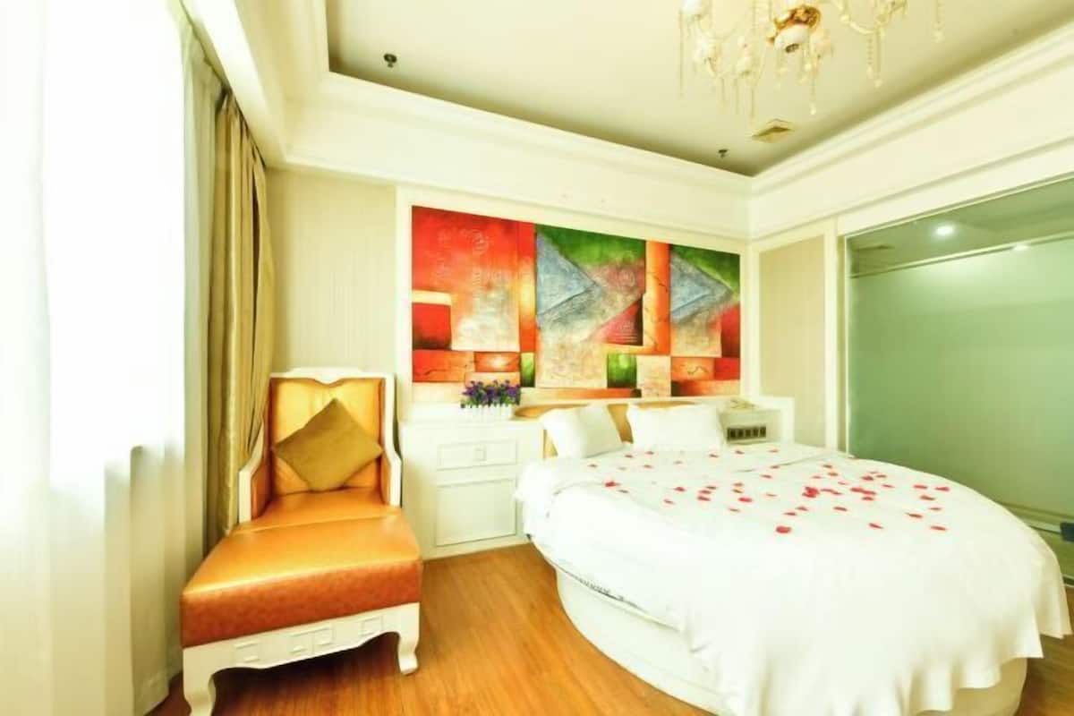 Quarto de hotel com uma cama grande, uma cadeira, uma cômoda e um quadro na parede.