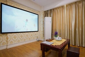 Quarto com uma grande televisão de tela plana na parede, geladeira branca, mesa de madeira com um vaso de flores e janela com cortinas.