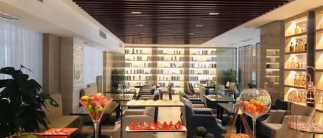Um saguão de hotel com balcão de recepção, área de estar e mesa de buffet com diversos alimentos.