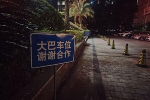 Cena de rua à noite, com uma placa azul na calçada, pavimento de tijolos e cones de trânsito amarelos.